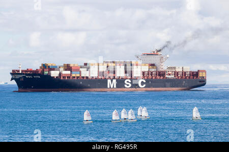Container ship emitting black smoke passing small sailing boats as it ...