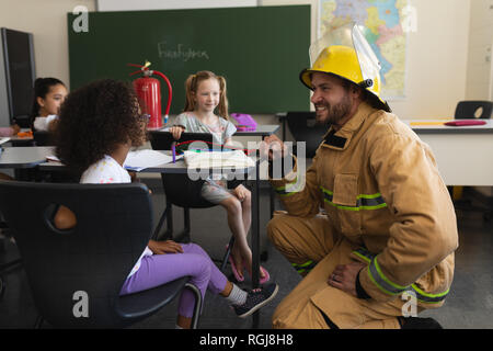 Side view of male Caucasian firefighter teaching schoolkids about fire ...