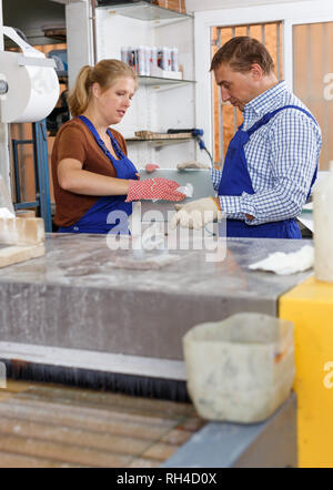 Male glazier with female assistant working on curved glass beveling ...