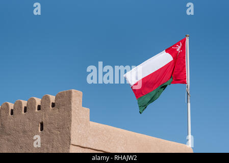 National flag of Oman flying from pole on top of old fort close to ...
