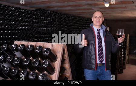 Male winemaker giving tour around winery, showing wine cellar with wine ...