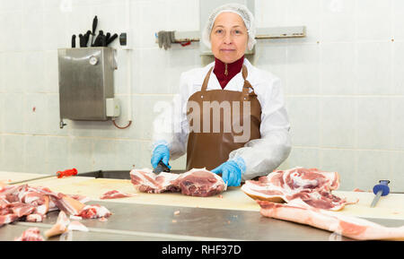 Portrait of skilled female worker cutting raw meat in meat packing ...