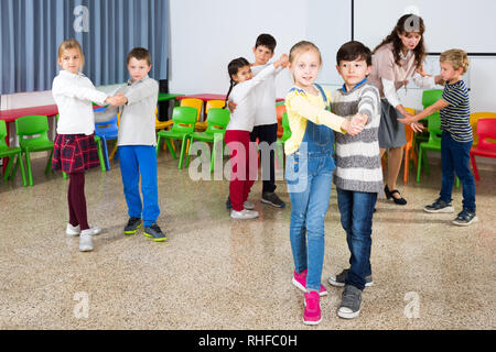 Happy kids and female teacher dancing together in classroom at ...