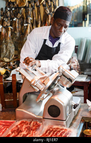 African American seller slicing jamon fixed on jamonera, preparing for ...