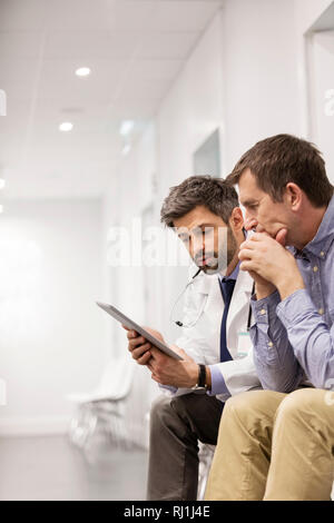 Doctor explaining mature patient over tablet PC while sitting on sofa ...
