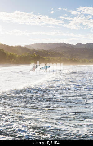 Two young women with surfboards wading in water Stock Photo - Alamy
