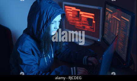 Girl hacker in a hood typing program code while committing a cybercrime hacking a system ...