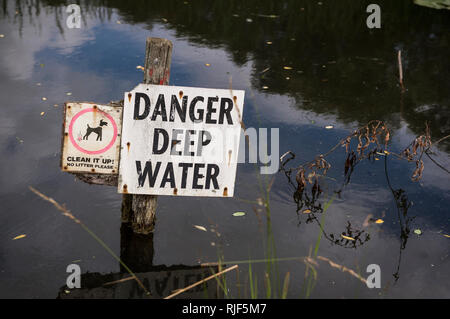 Pond warning signs in a park on a wooden post advising of deep water ...