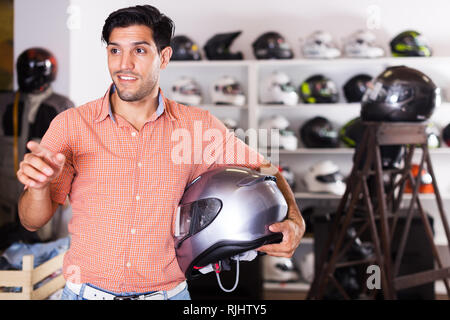Smiling man is choosing moto helmet for head protection in sport shop ...