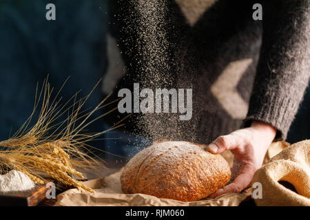 Man with fresh bread and wheat spikelets on light background, closeup ...