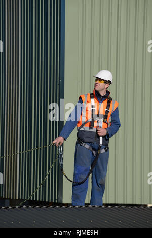 A builder wearing a safety harness while working at heights waits for ...