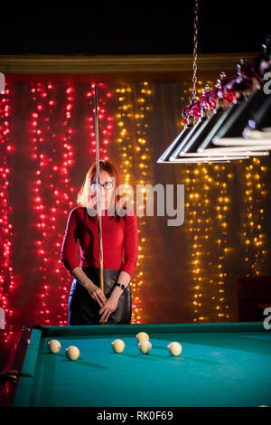 Billiard club. A woman with red hair standing by the table holding a ...