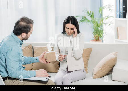 psychotherapist with clipboard giving paper tissues to upset young ...