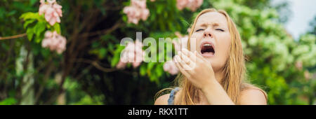 Young woman sneezes in the park against the background of a flowering ...
