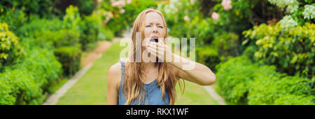 Young woman sneezes in the park against the background of a flowering ...