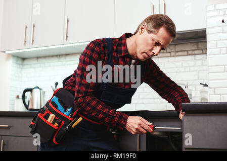 Handyman at work. Repairing kitchen shelves with cordless screwdriver ...