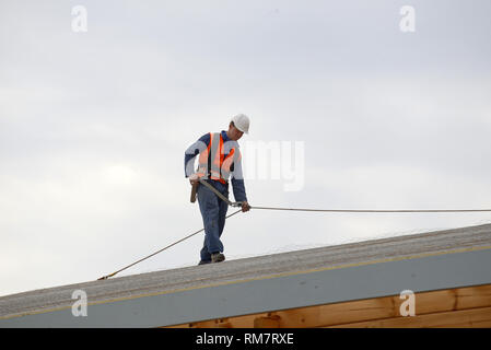A builder secures safety lines for men about to put the roof on a large ...