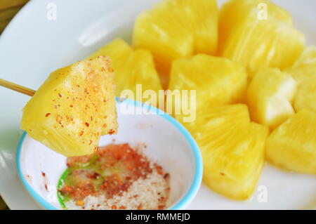 pineapple slice dipping with mixed sugar salt and pepper on white plate ...