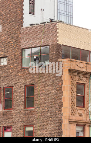 Industrial engineer rappelling down the side of a building on a ...