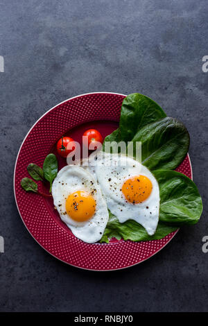 Two heart-shaped fried eggs on a black ceramic plate on a dark concrete ...