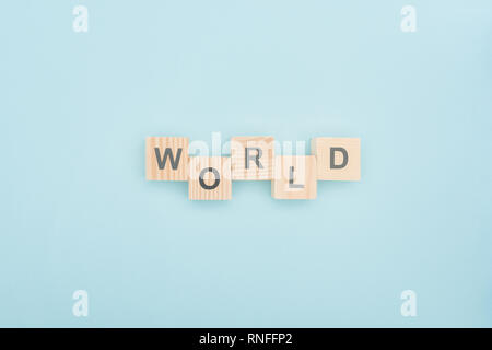 top view of wooden cubes with travel lettering and straw hat on blue ...