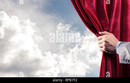 Cloudy landscape behind red curtain and hand holding it Stock Photo - Alamy