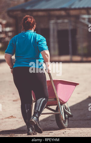 Woman pushing empty wheelbarrow Stock Photo - Alamy