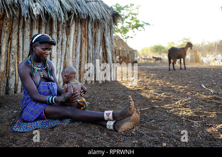 Beautiful young woman of Zemba tribe in traditional clothing cooks ...