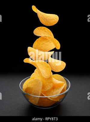 Potato chips falling into glass bowl isolated on white background with ...