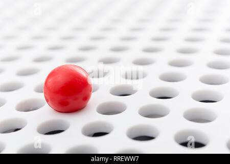 Abstract holes. Small solitary red plastic ball isolated on round holed ...
