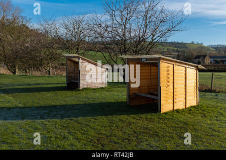 Two small rustic football dugouts in a field, with a clear blue sky in ...