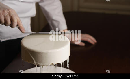 Confectioner fills cakes with white liquid glaze. She equals top ...