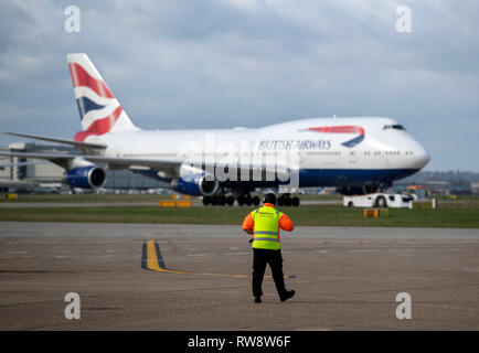A airside operations member of staff guides in planes at Heathrow ...