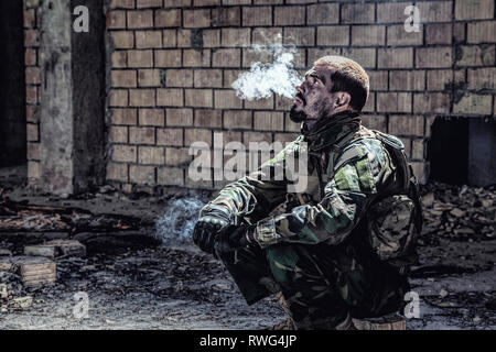 Special forces soldier smoking a cigarette while sitting in a ruined ...