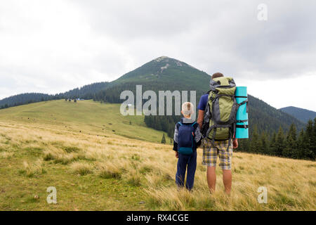 Dad and son child with tourist backpacks at low wooden fence on green ...