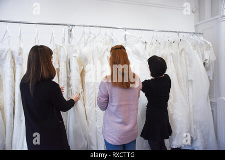2 shop assistants are helping a pretty red haired girl in a Wedding ...