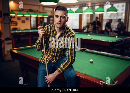 Male billiard player with cue poses at the green table. Man plays ...