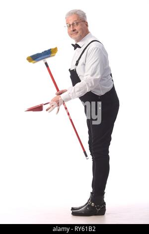Gray-haired cleaner, janitor in a black jumpsuit with a mop and dustpan ...