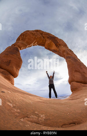 Delicate arch in the winter with a hiker standing at the base of to ...