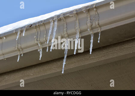 Close upward view of Icicles dripping from a snow filled roof rain ...