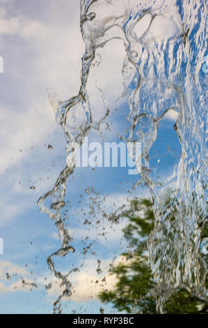 transparent falling water vertical flows against a blue sky and green ...