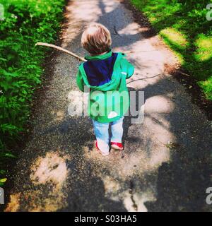 Rear-view of boy with walking stick walking in nature with his father ...