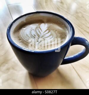 Cup of cappuccino coffee with Rosetta latte art stands on a wooden desk ...
