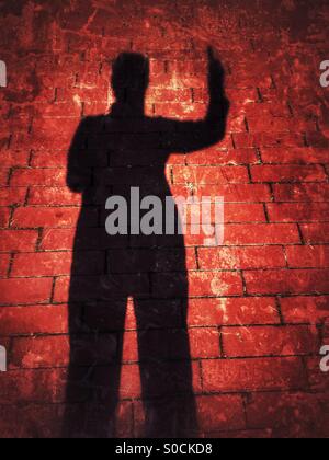 Shadow silhouette selfie of person pointing to the right, over brick ...
