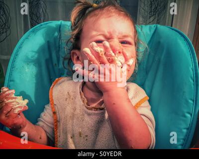 Eating baby girl with messy face. The nice one-year child eats and ...