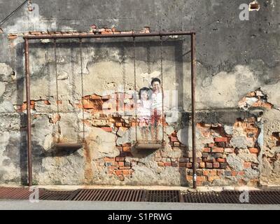 Street art art brother and sister on a swing on a wall in George Town on Penang Island in ...