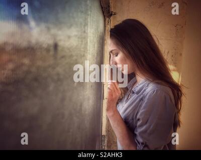 Sad woman leaning against the window Stock Photo - Alamy