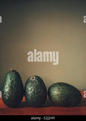 Still life of three avocados on a wooden surface with grey background ...