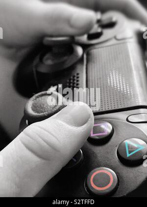 A white hand holding a Playstation controller against a black ...