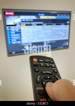 Person pointing a TV remote and pressing buttons in front of a TV with ...